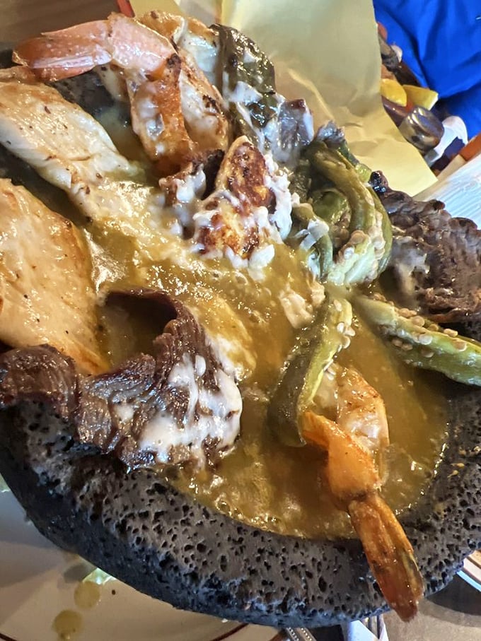 The molcajete arrives like a volcanic eruption of flavor – meat, shrimp, and vegetables swimming in savory sauce within a traditional stone bowl.