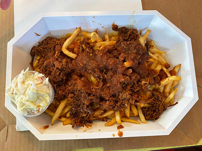 Pulled pork fries—a glorious mountain of crispy potatoes buried under tender meat and sauce, with coleslaw standing by to cool the flavor avalanche.