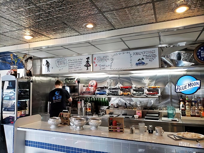 The kitchen area showcases handwritten specials and that impressive model car collection. Every detail speaks to decades of diner tradition.
