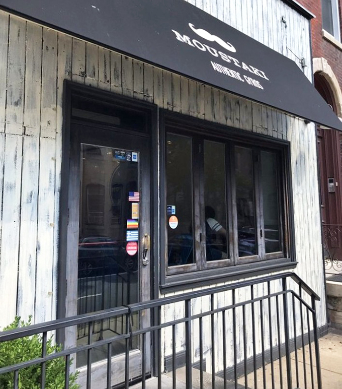 The distinctive black awning with its playful mustache logo serves as a beacon for those seeking authentic Greek street food.