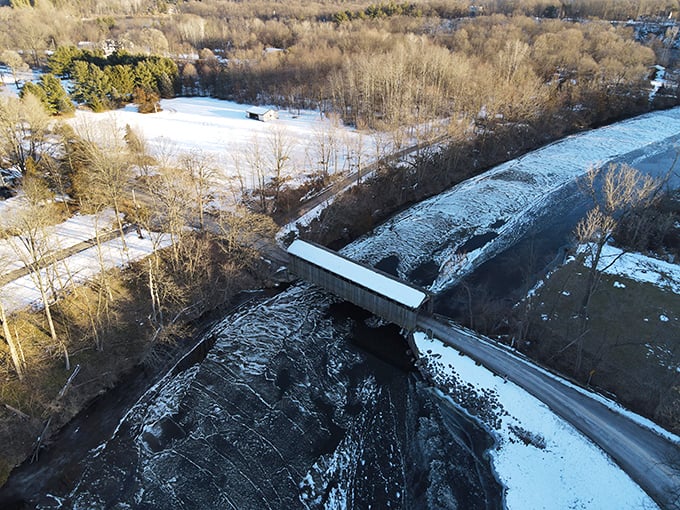 Winter's blanket drapes the landscape, revealing the bridge's perfect geometry against the snow-covered terrain in this breathtaking aerial view.