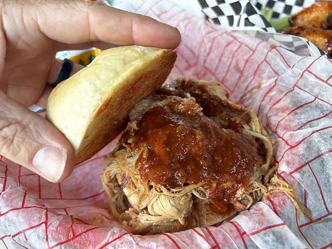 This pulled pork sandwich stacks high like architectural achievement, demanding both hands and serious napkin commitment.