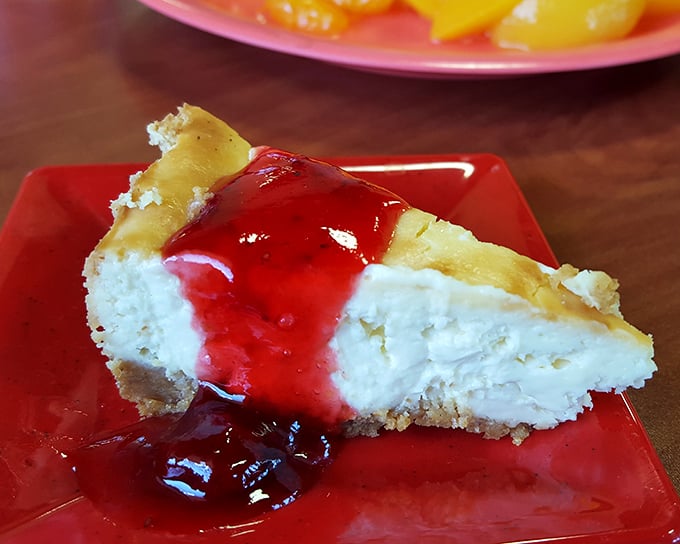 Cheesecake topped with ruby-red strawberry sauce – where cream cheese transcends to dessert divinity on a graham cracker throne.