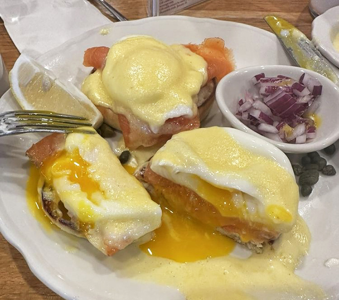 Eggs Benedict with hollandaise cascading like a yellow waterfall—breakfast's answer to formal wear, with a side of chopped onions.