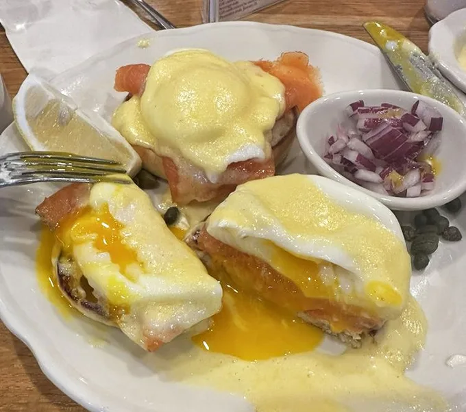 Eggs Benedict with hollandaise cascading like a yellow waterfall—breakfast's answer to formal wear, with a side of chopped onions.
