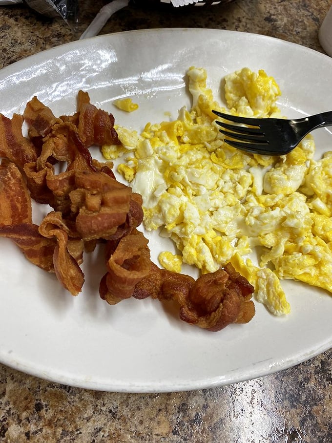 Breakfast fundamentals executed with precision—eggs scrambled to fluffy perfection alongside bacon that's achieved that mythical balance between crisp and chewy.