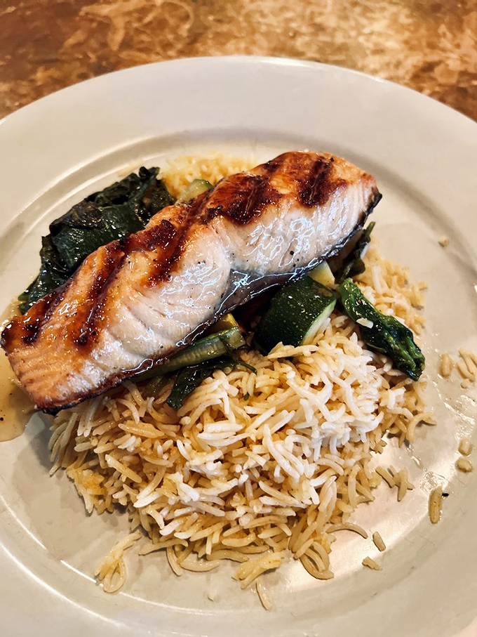 Perfectly grilled salmon resting on a bed of rice and vegetables – proof that sometimes the simplest preparations yield the most magnificent results.