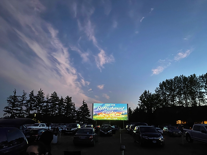 As twilight fades to darkness, the screen illuminates with pre-show advertisements—that magical moment when cars become personal theaters under Oregon skies. 