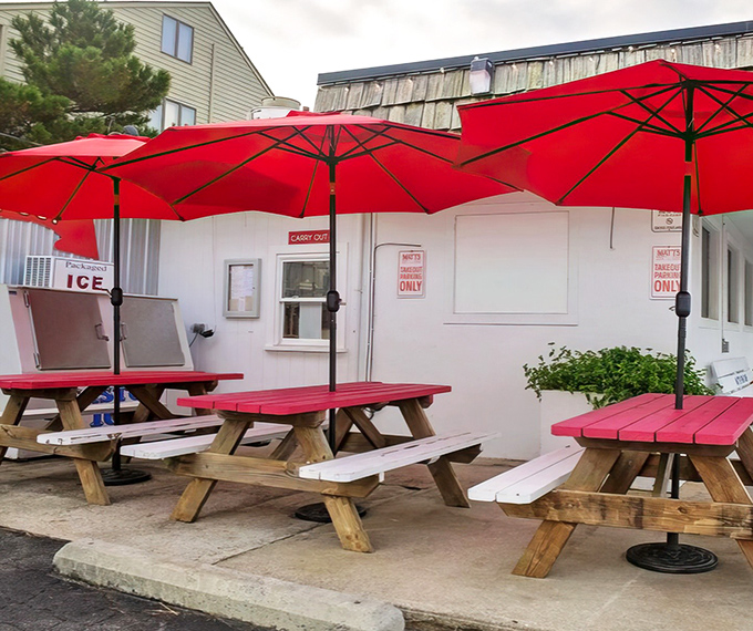 Outdoor picnic tables under cherry-red umbrellas—where the sea breeze serves as nature's appetizer before the main event.