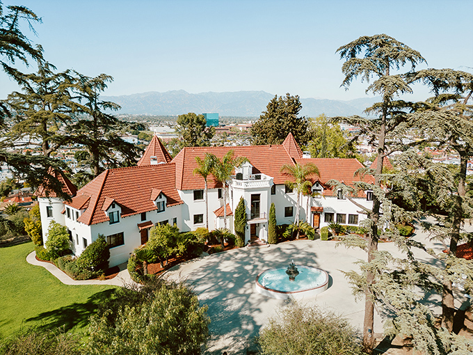 The castle reveals its full splendor from above, where red-tiled turrets and manicured grounds create a fairytale setting in suburban California.