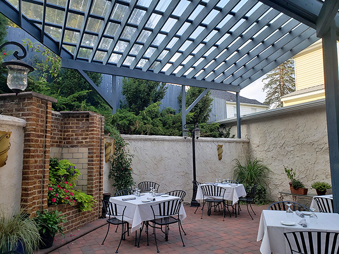 Dine al fresco under the pergola where brick, white walls, and carefully placed greenery create an outdoor room that feels both intimate and airy.