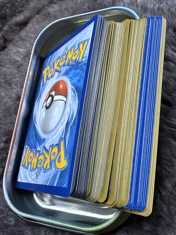 Pokémon cards nestled in their metal tin—where childhood nostalgia meets adult collecting obsession in a perfect storm of "gotta catch 'em all."