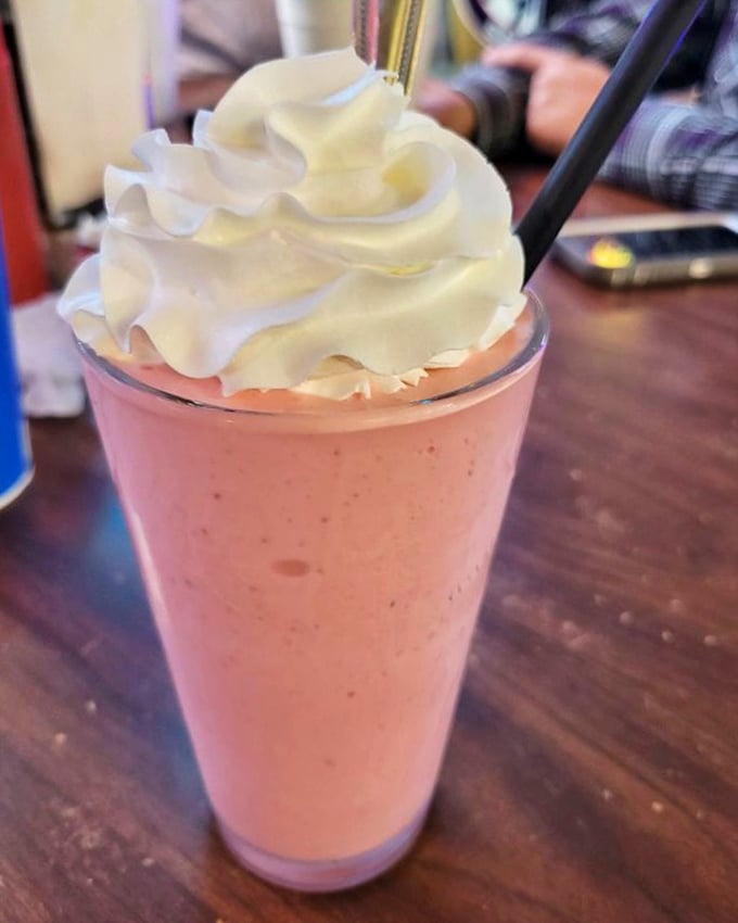 The strawberry shake arrives like a pink cloud topped with whipped cream – childhood nostalgia in a glass that tastes like summer.