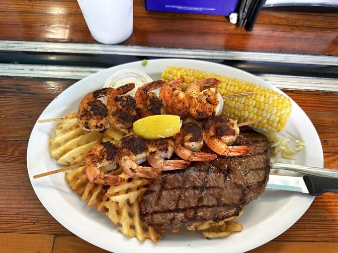 Land meets sea in perfect harmony – blackened shrimp skewers and a juicy steak sharing real estate with golden waffle fries.