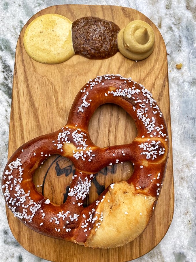The Bavarian pretzel arrives on a wooden board with three mustard varieties—a carb-lover's dream that puts mall pretzels to absolute shame.