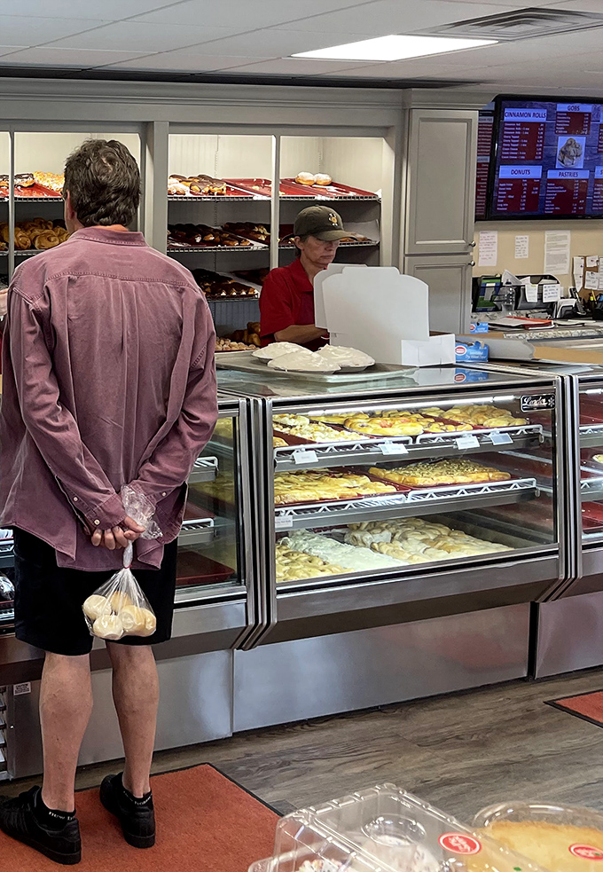 The sacred transaction – a customer clutches his bag of donuts like precious cargo while the staff prepares to make another food dream come true.