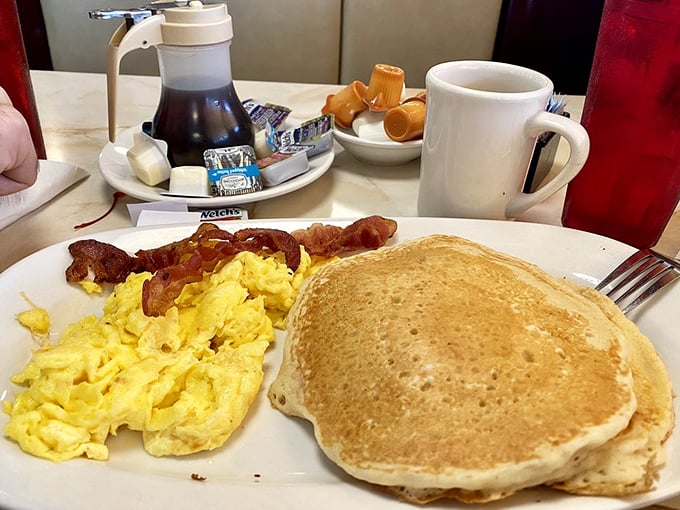 The breakfast that launched a thousand productive days—golden pancakes alongside perfectly scrambled eggs and bacon that shatters like glass.