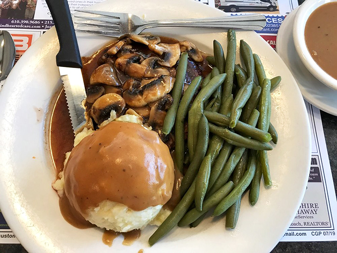 A plate of salisbury steak swimming in mushroom gravy—the kind of meal that makes you want to hug the chef afterward.