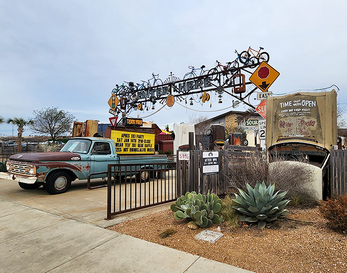 The eclectic entrance features vintage vehicles, bicycles mounted overhead, and desert landscaping—setting the tone for the wonderfully weird experience within.