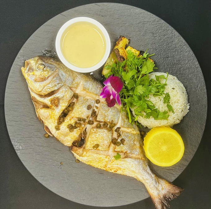 Whole fish perfection with capers, lemon, and that orchid garnish saying "Yes, I'm fancy." Simple preparation letting the ocean's flavor shine through.
