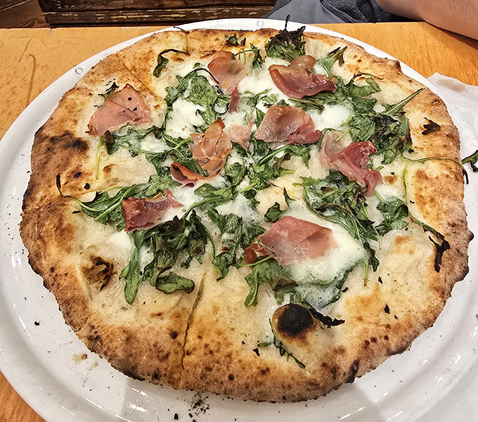A pizza that defies expectations—thin crust, prosciutto, and fresh greens creating a harmony that would make even Italian nonnas nod in approval.