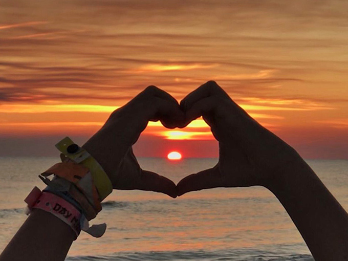 Hands forming a heart against a fiery sunset—the universal symbol for "sorry boss, I'm extending my vacation another week."
