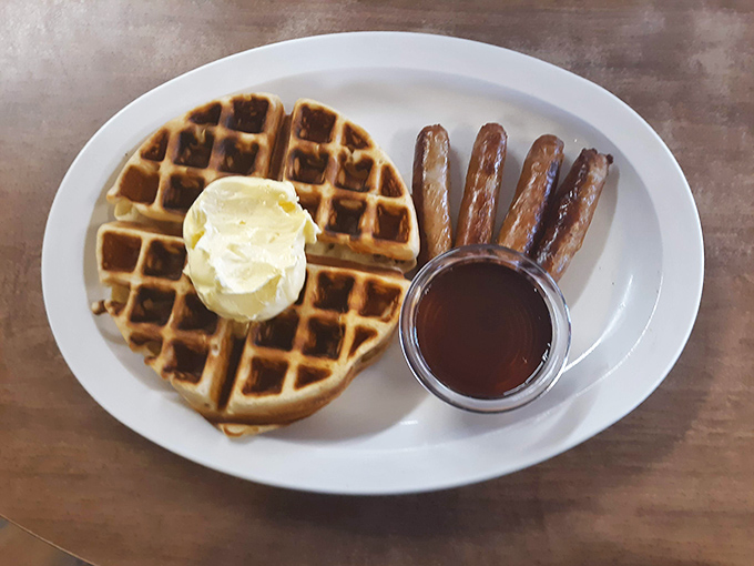A golden waffle with a perfect butter crown and sausage sentries standing guard—breakfast royalty that costs less than your fancy coffee drink.