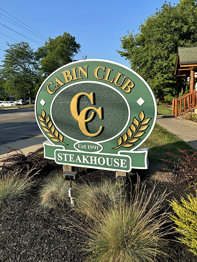 The Cabin Club sign stands like a friendly sentinel, promising steakhouse treasures within its log cabin kingdom just off the suburban roadway.