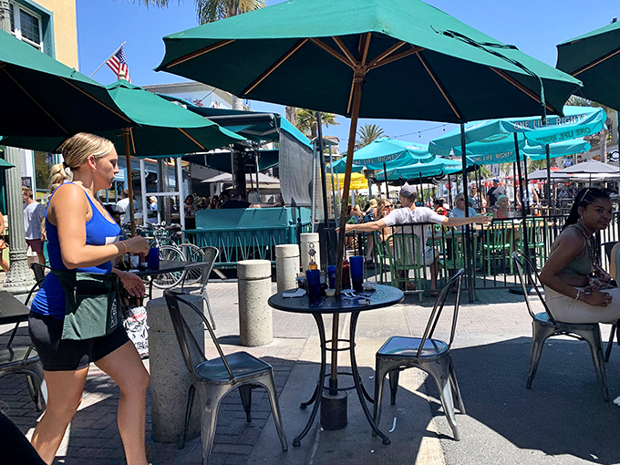The outdoor patio buzzes with the energy of beach-goers fueling up for the day. Those green umbrellas provide shade for what might be the most important meal decision of your vacation.