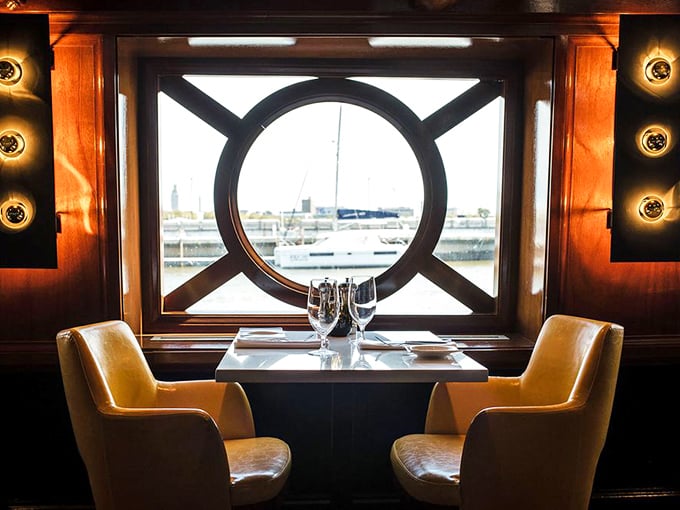 Porthole dining for two—where intimate conversations are framed by circular windows to the water world beyond, creating private moments in a setting that's gloriously cinematic.
