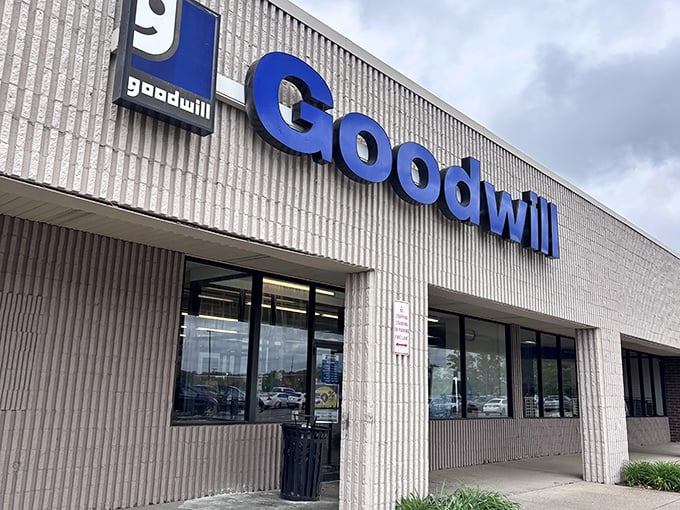 The iconic blue Goodwill sign beckons like a lighthouse for bargain hunters navigating the sea of retail.