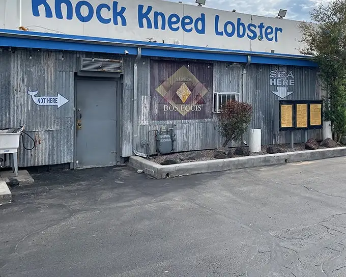 The "NOT HERE" sign points elsewhere, but trust me—this weathered blue-trimmed building is exactly where your seafood cravings need to be.