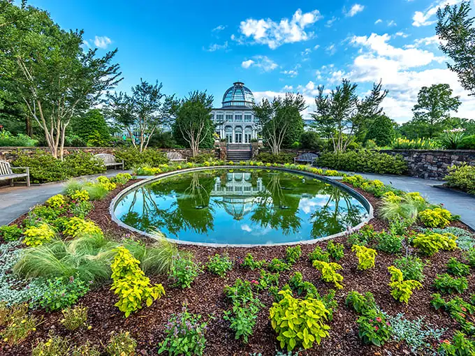 Nature's perfect mirror: the Conservatory reflects in the circular pond, creating a double dose of architectural splendor surrounded by vibrant plantings.