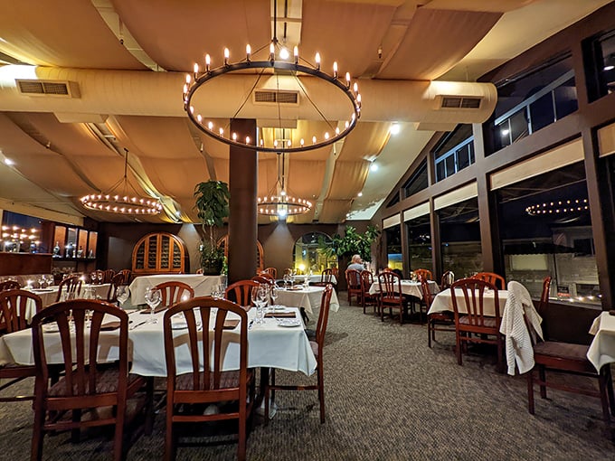 Circular chandeliers hover like modern halos above white-clothed tables, creating an atmosphere where casual coastal charm meets upscale dining without pretension.