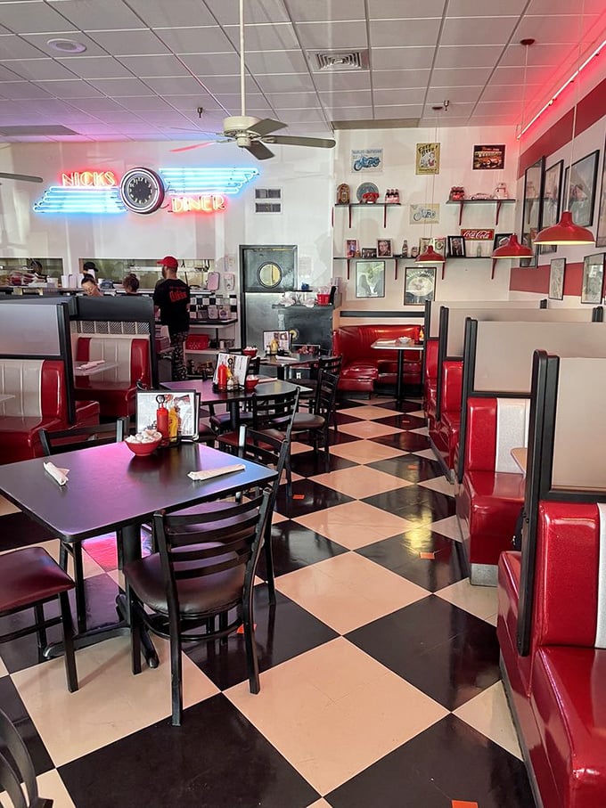Classic black-and-white floors and cherry-red booths create the perfect backdrop for comfort food conversations. The neon glow promises good things ahead.