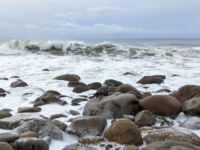 Nature's mosaic of smooth stones meets frothy waves in a timeless dance. The Pacific doesn't just crash here—it converses with the ancient coastline.
