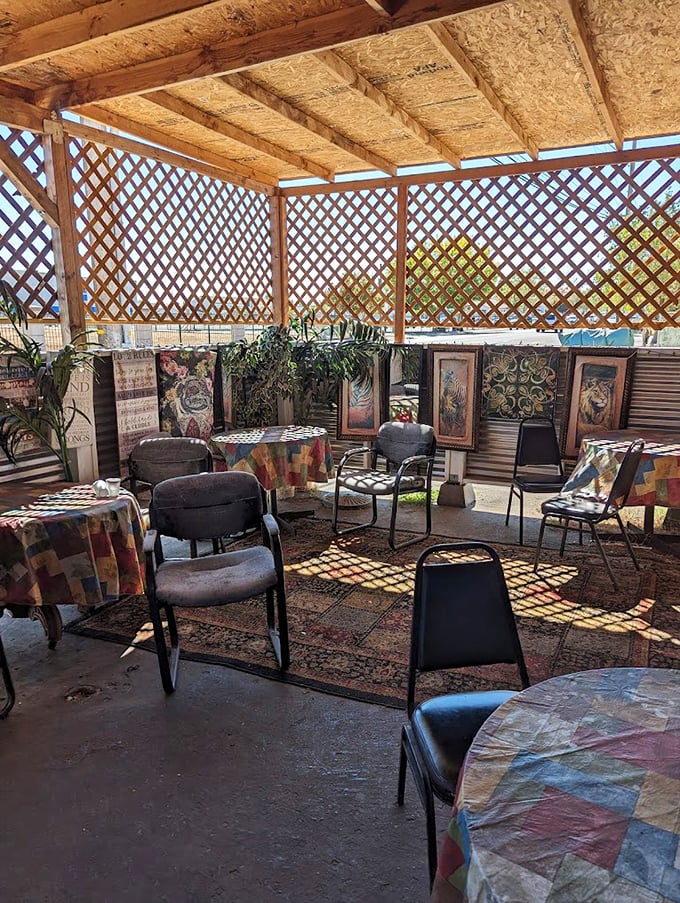 Dappled sunlight filters through wooden lattice in the outdoor seating area, where colorful tablecloths and framed artwork create an unexpectedly cozy dining atmosphere.
