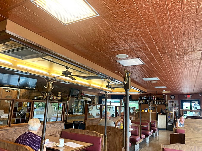 Classic diner aesthetics meet comfort in this interior where ornate ceiling tiles and burgundy booths create the perfect backdrop for morning rituals.