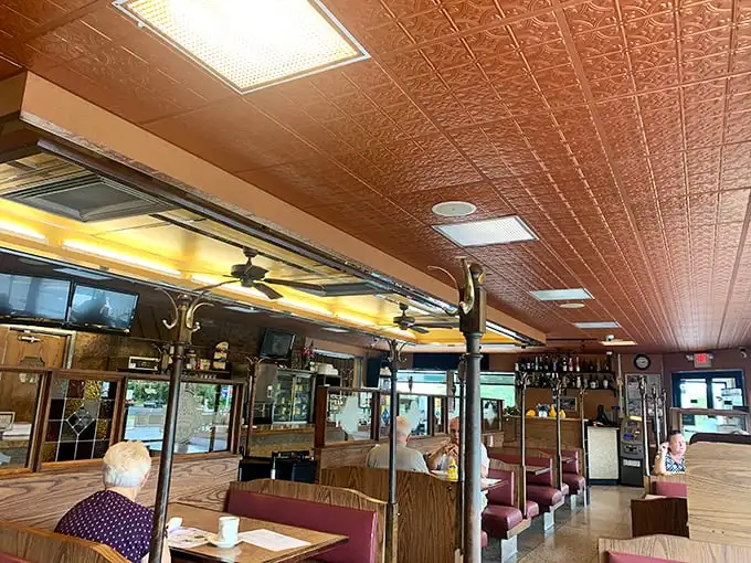 Classic diner aesthetics meet comfort in this interior where ornate ceiling tiles and burgundy booths create the perfect backdrop for morning rituals.