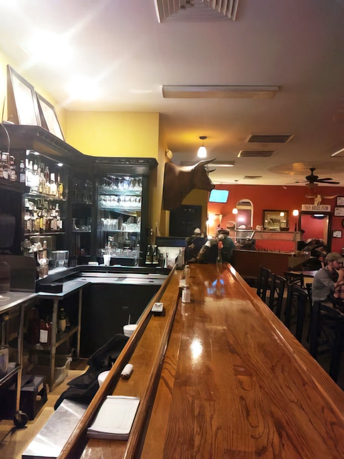 The gleaming wooden bar isn't just furniture—it's a front-row seat to the steakhouse symphony that unfolds nightly.