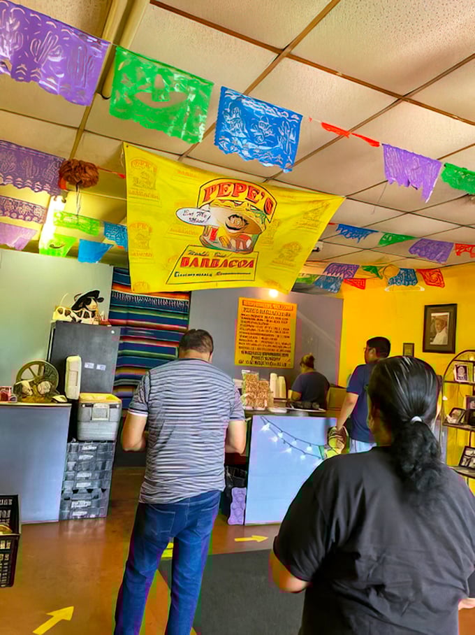 Colorful papel picado creates a festive canopy over customers eagerly awaiting their barbacoa destiny at the counter.
