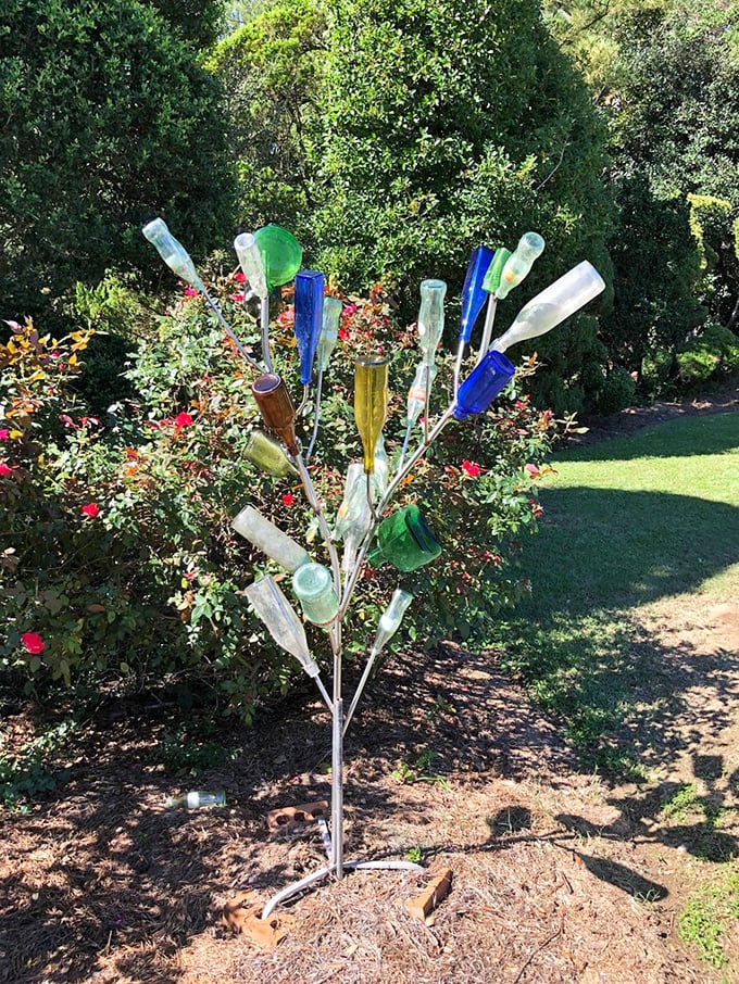 Southern folk art meets horticulture—this bottle tree captures sunlight in colored glass while surrounded by meticulously shaped greenery.