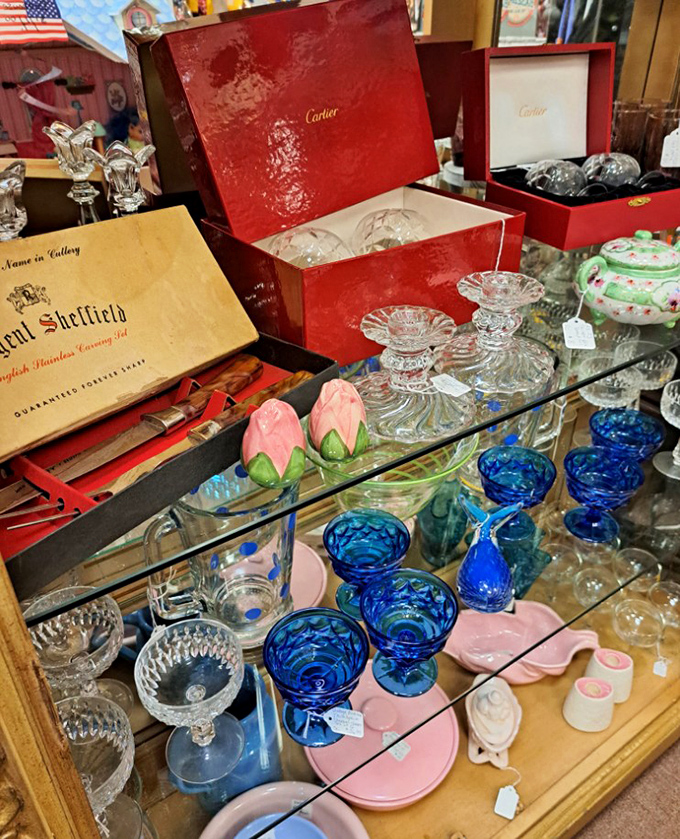 These aren't just drinking vessels – they're liquid jewels. Cartier boxes and Sheffield cutlery sharing space with cobalt blue goblets that practically sing in the light. 