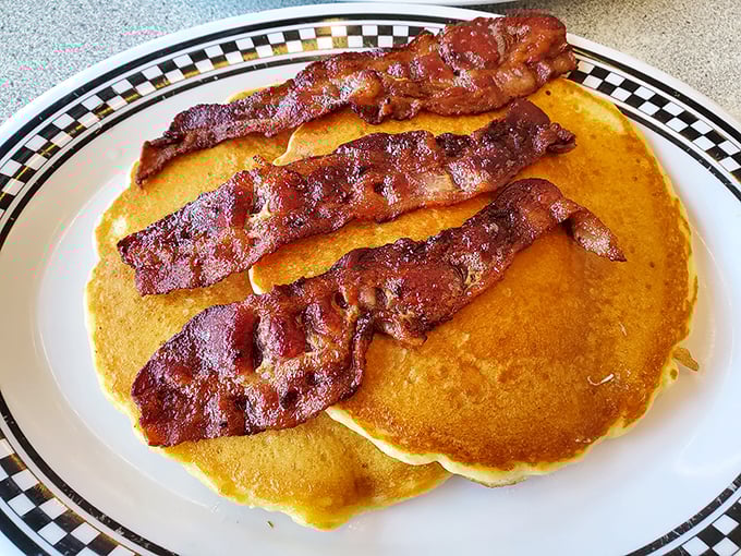 Golden pancakes supporting crispy bacon strips—a breakfast alliance so perfect it should have its own national holiday or at least a dedicated fan club.