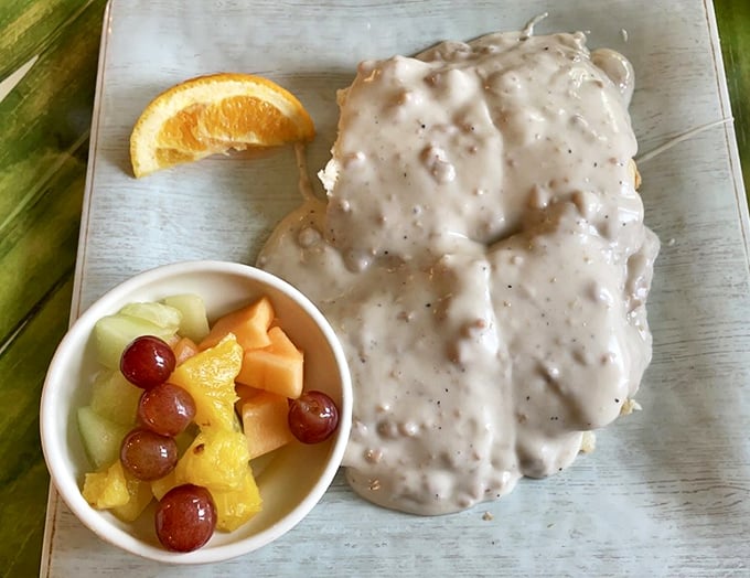 Biscuits swimming in creamy gravy alongside fresh fruit—proof that indulgence and virtue can peacefully coexist on the same plate.