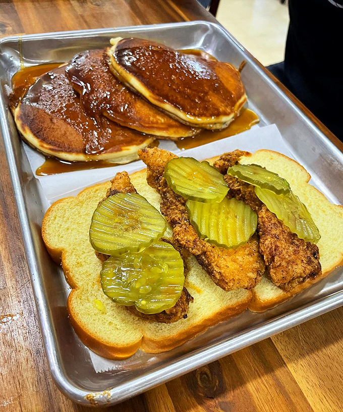 Pancakes drowning in syrup next to fried chicken on white bread with pickles—breakfast and lunch having a delicious identity crisis that works magnificently.