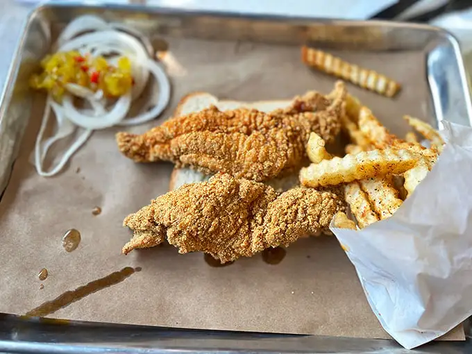 Golden-brown catfish strips with the perfect cornmeal crust alongside crispy fries. This isn't just lunch—it's edible sunshine on a metal tray.