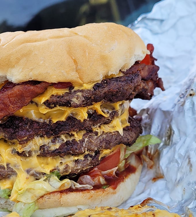 Behold the triple-decker masterpiece that laughs in the face of dainty appetites. This isn't just a burger – it's an architectural achievement with cheese as its mortar.