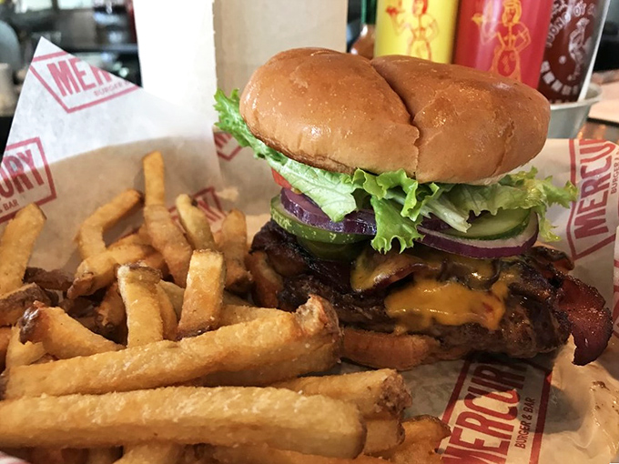 Behold the burger in its natural habitat—juicy, perfectly stacked, and flanked by golden hand-cut fries. Napkins required, not optional.