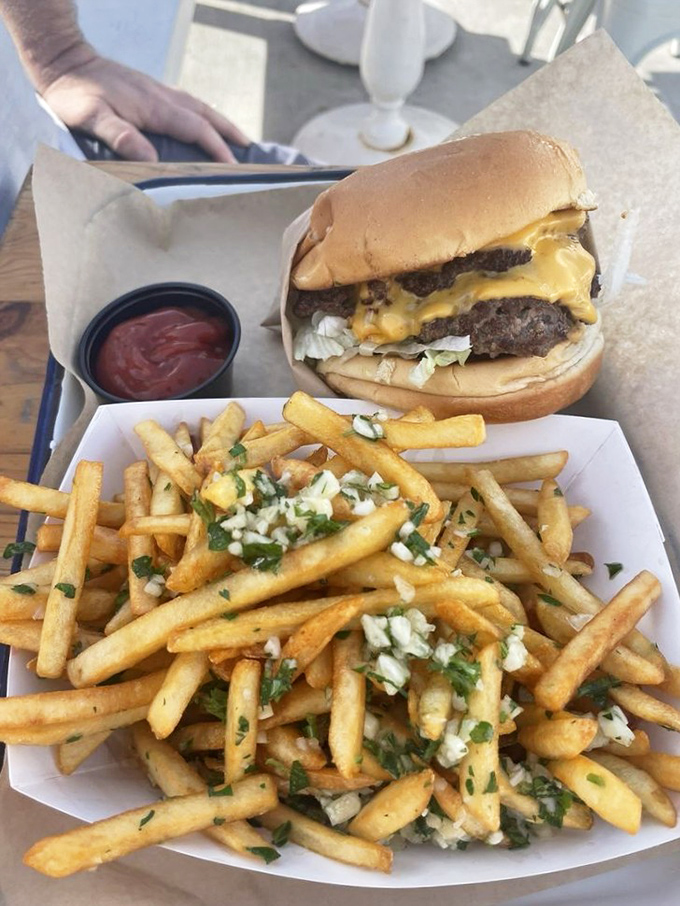 This isn't just a cheeseburger—it's edible architecture with a golden foundation of perfectly crisp, herb-flecked fries that demand to be savored one by one.